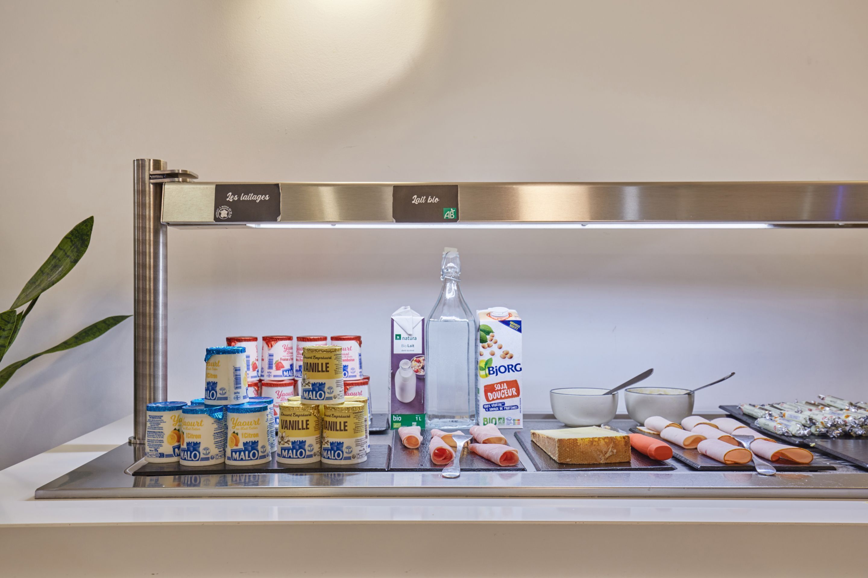 Buffet com diversos alimentos, incluindo iogurte, leite e cachorros-quentes.
