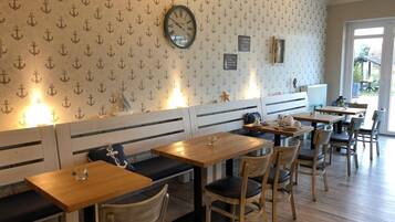 Restaurante com tema náutico, mesas e bancos de madeira, um relógio na parede e vista para o exterior.