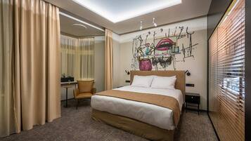 Quarto de hotel com uma cama grande, uma escrivaninha, uma cadeira e uma luminária no teto.
