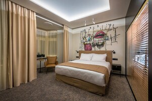 Quarto de hotel com uma cama grande, uma escrivaninha, uma cadeira e uma luminária no teto.