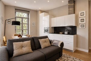 Uma sala de estar moderna com sofá, mesa de jantar e área de cozinha com armários brancos e bancada preta.