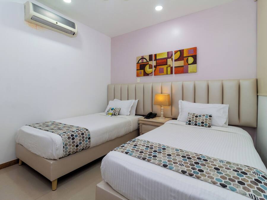 Quarto de hotel com duas camas, ar condicionado fixado na parede e mesa de cabeceira com abajur.