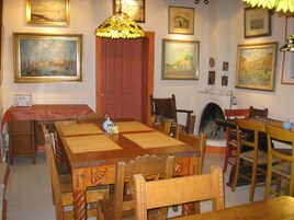 Uma sala de jantar com mesa de madeira, cadeiras, uma porta vermelha e diversas obras de arte emolduradas nas paredes.