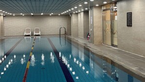 Piscina interna com divisórias de pista bem definidas, piso em azulejo e teto com iluminação embutida.