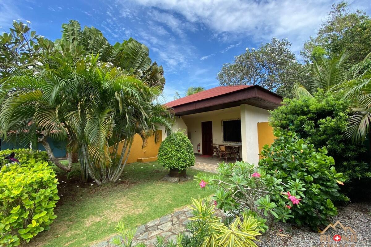 Uma casa com telhado vermelho, rodeada por vegetação exuberante e um jardim bem cuidado.