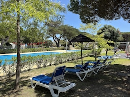 Uma área à beira da piscina com espreguiçadeiras e um guarda-sol de palha.