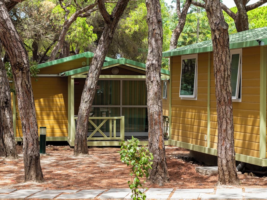 Fileira de cabanas amarelas com telhados verdes, rodeadas por árvores.