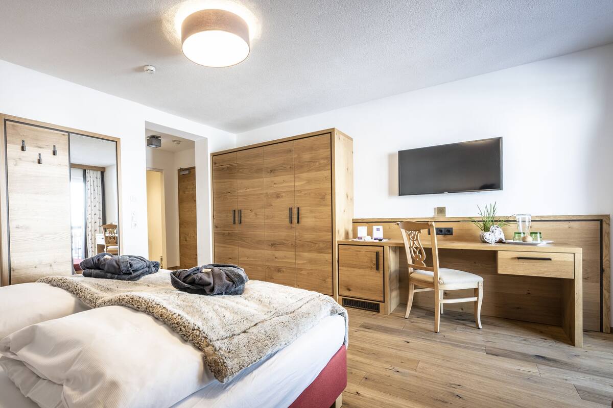 Quarto de hotel moderno com cama, escrivaninha, cadeira, televisão e guarda-roupa.