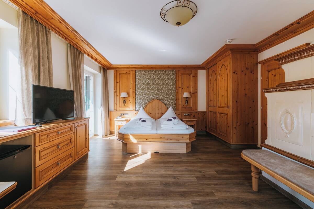 Quarto com cama de madeira, televisão e um banquinho.