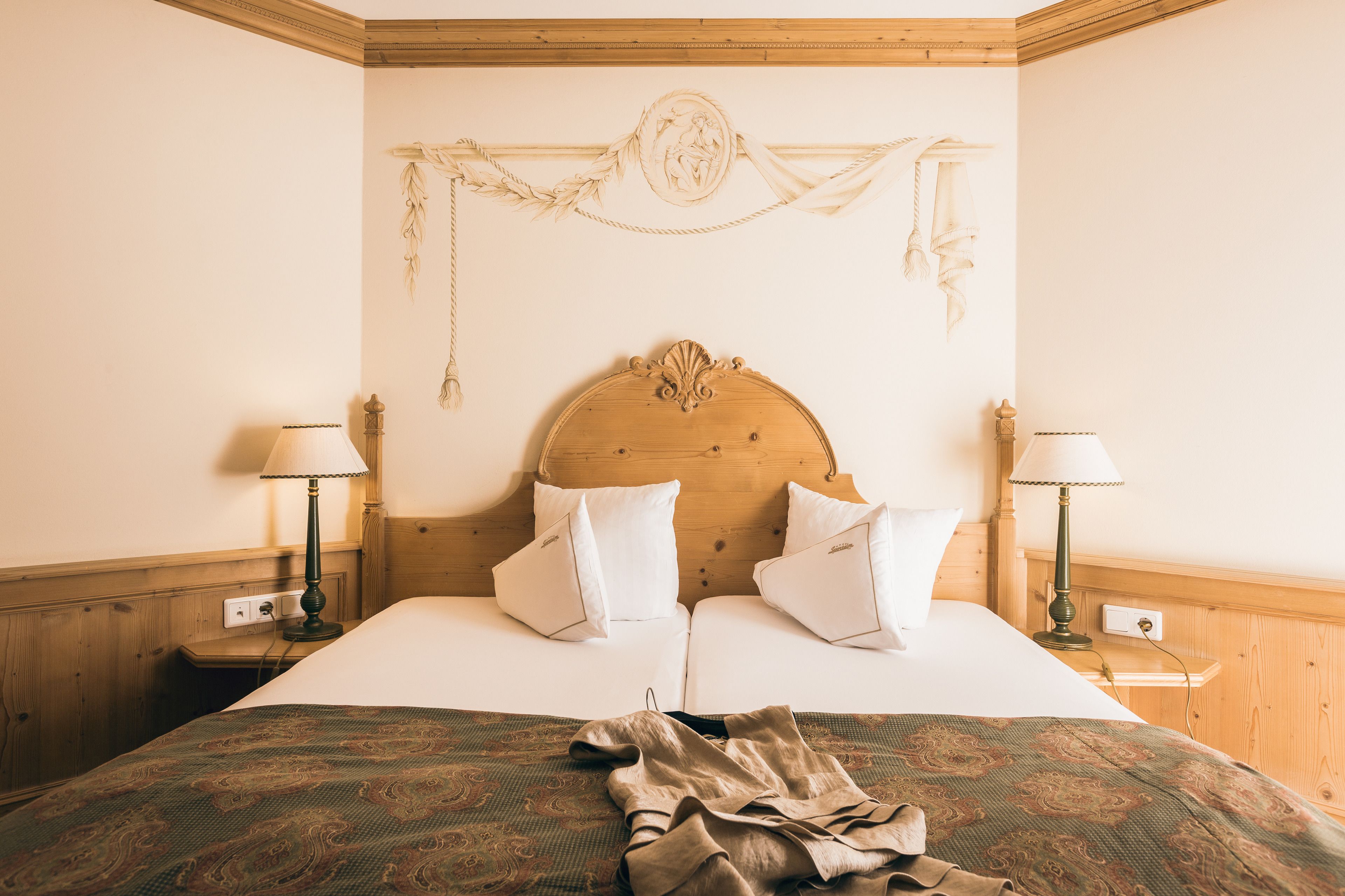 Cama bem arrumada com colcha estampada, duas luminárias de cabeceira e um painel decorativo.