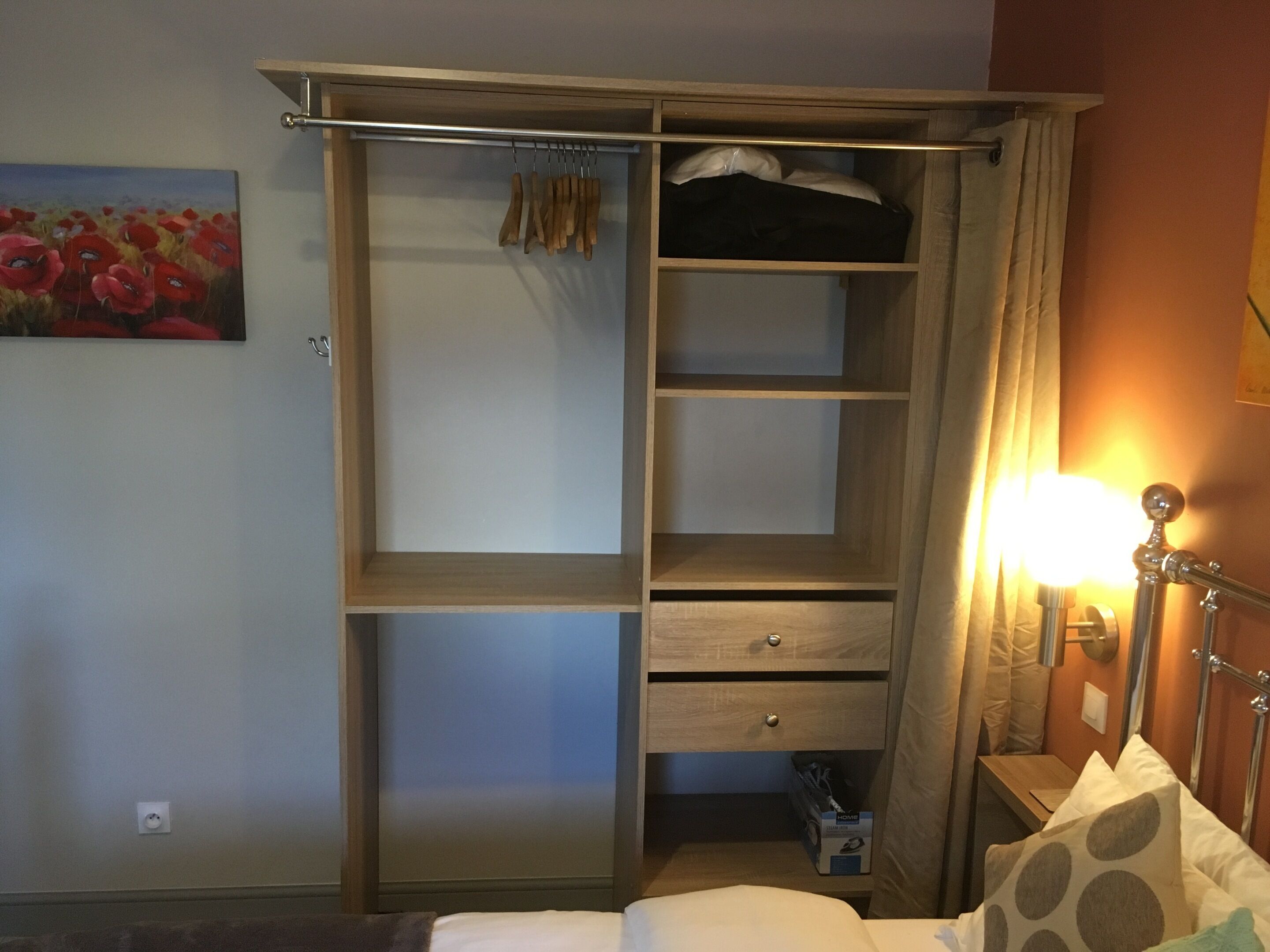 Quarto com guarda-roupa de madeira, cama com roupa de cama branca e pintura de flores vermelhas na parede.