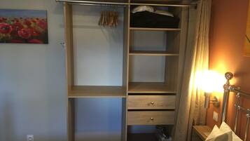 Quarto com guarda-roupa de madeira, cama com roupa de cama branca e pintura de flores vermelhas na parede.
