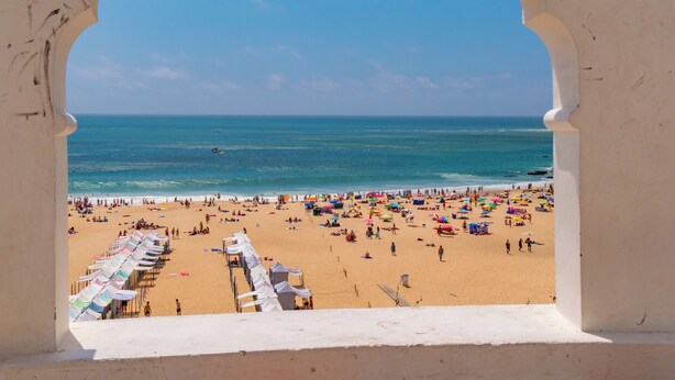 Vista da praia através de um arco, com tendas e guarda-sóis.