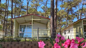 Uma cabana pequena, térrea, com telhado vermelho e uma varanda, rodeada por árvores.