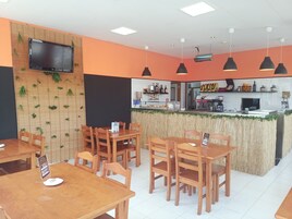 Um restaurante com mesas e cadeiras de madeira, um balcão com um cardápio e uma televisão na parede.
