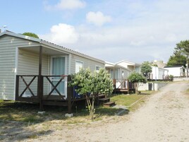 Uma fileira de casas móveis com varandas, um caminho de terra e vegetação rala.