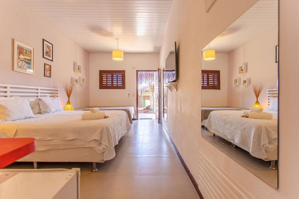 Quarto de hotel com duas camas, um espelho, um corredor e uma porta que dá para o exterior.