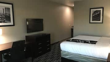 Quarto de hotel com cama, escrivaninha, cadeira, televisão e um quadro na parede.