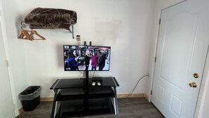 Quarto com televisão em móvel, cabideiro, porta e lixeira.