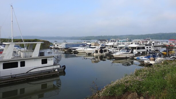Marina com vários barcos atracados, água calma e paisagem montanhosa ao fundo.