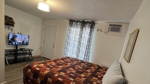 Quarto com uma cama, televisão e janela com cortinas.