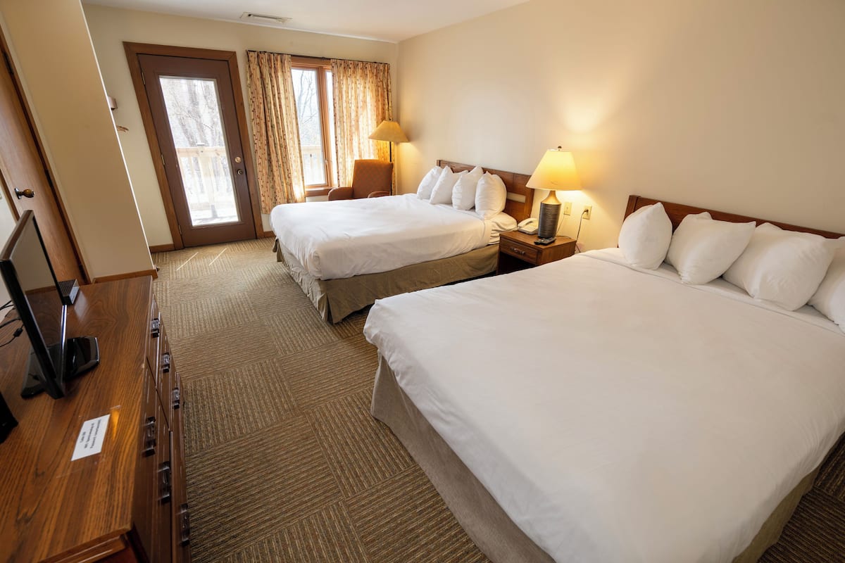 Quarto de hotel com duas camas, uma escrivaninha com computador e uma janela com cortinas.