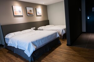 Quarto de hotel com duas camas, uma cabeceira escura e três quadros na parede.