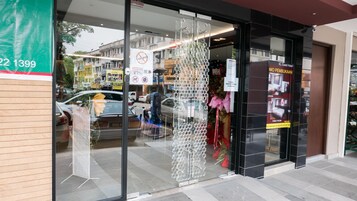 Entrada de hotel com porta de vidro, aviso indicando promoção e vista da rua com carros e edifícios.