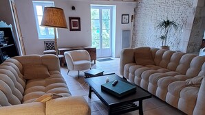 Uma sala de estar espaçosa com dois sofás bege, uma mesa de centro e uma luminária. Há uma janela com vista para o verde lá fora.