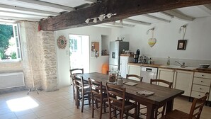 Uma área de refeições espaçosa com uma grande mesa de madeira e cadeiras, uma cozinha ao fundo e uma parede de pedra.