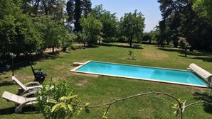 Uma piscina retangular rodeada por um relvado com árvores ao fundo.