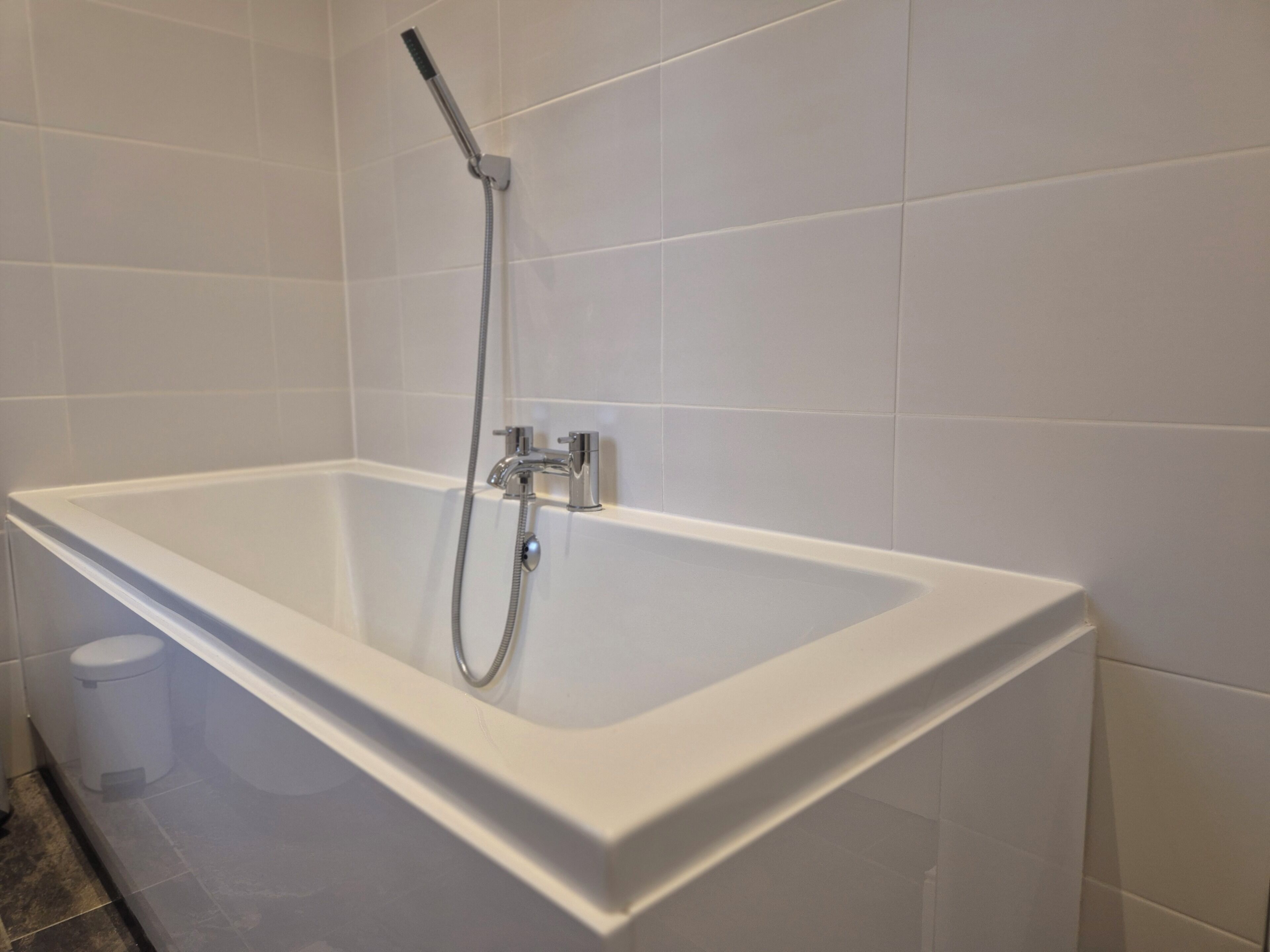 Uma casa de banho moderna com uma banheira branca, um chuveiro manual e uma sanita.