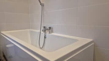 Uma casa de banho moderna com uma banheira branca, um chuveiro manual e uma sanita.