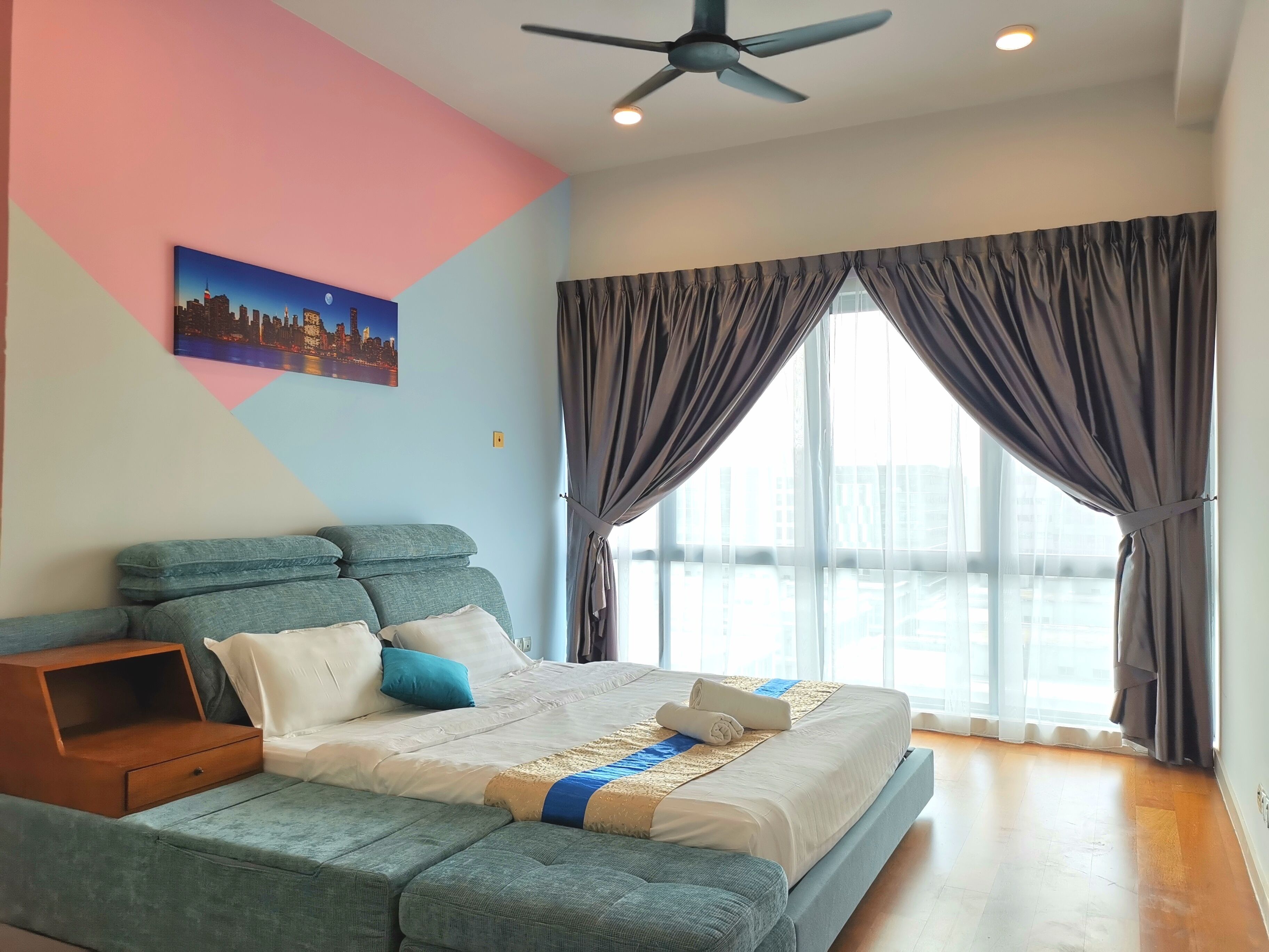 Quarto com cama, mesa de cabeceira, ventilador de teto e uma janela grande com cortinas.