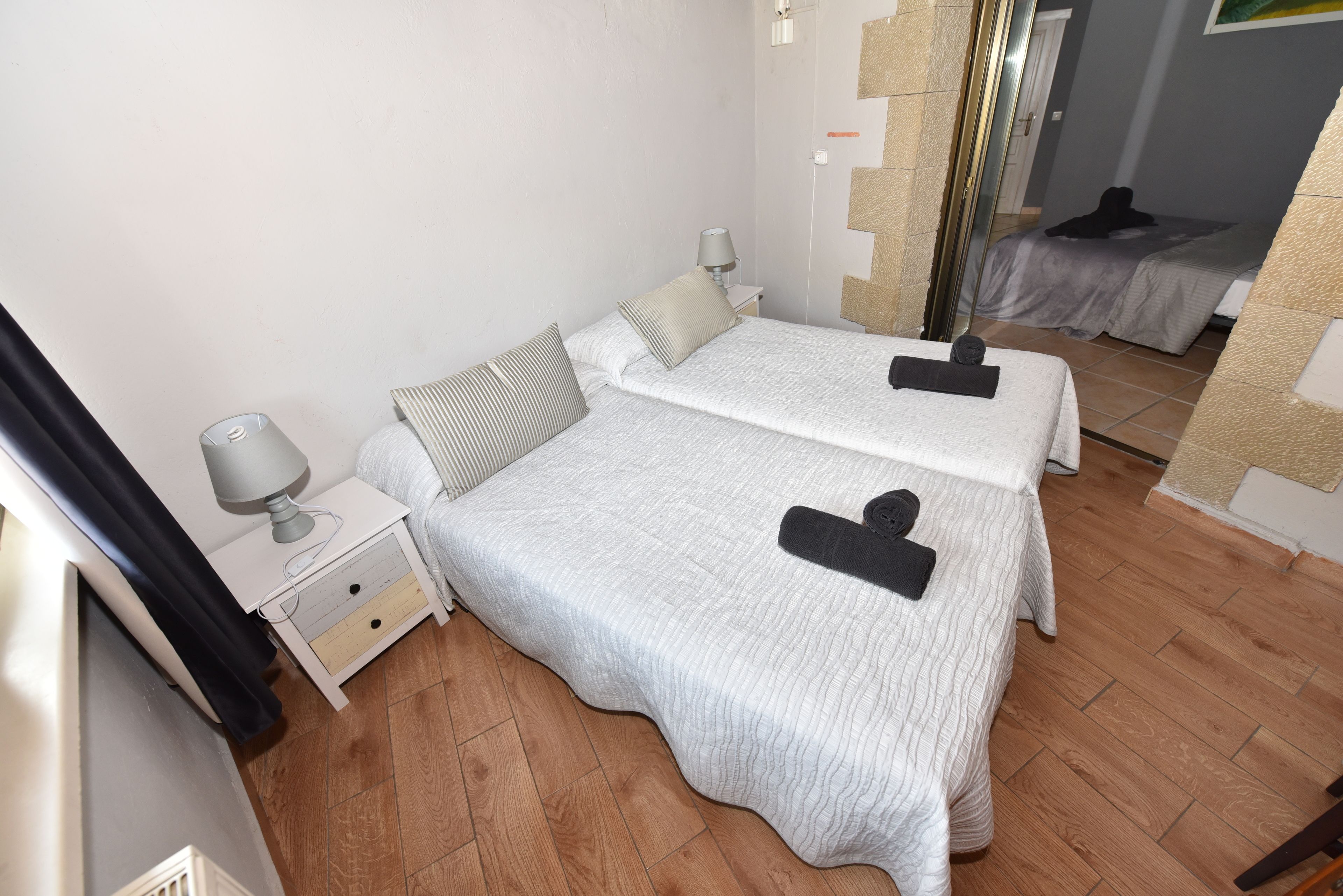 Quarto com duas camas, mesa de cabeceira com abajur e espelho.