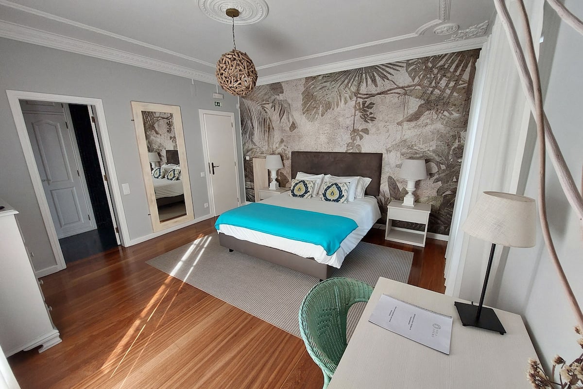 Quarto moderno com cama grande, piso de madeira e um mural decorativo na parede.