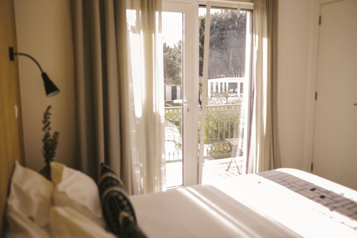 Quarto com cama, mesa de cabeceira e janela com cortinas.