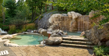 Área de fontes termais naturais com piscina, escadas que levam a uma cascata e vegetação exuberante ao redor.