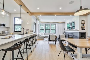 Uma cozinha moderna com uma ilha central, banquetas de bar e uma área de jantar com mesa e cadeiras de madeira.