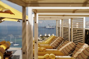 Varanda com poltronas de descanso amarelas e vista para o mar e um navio de cruzeiro.