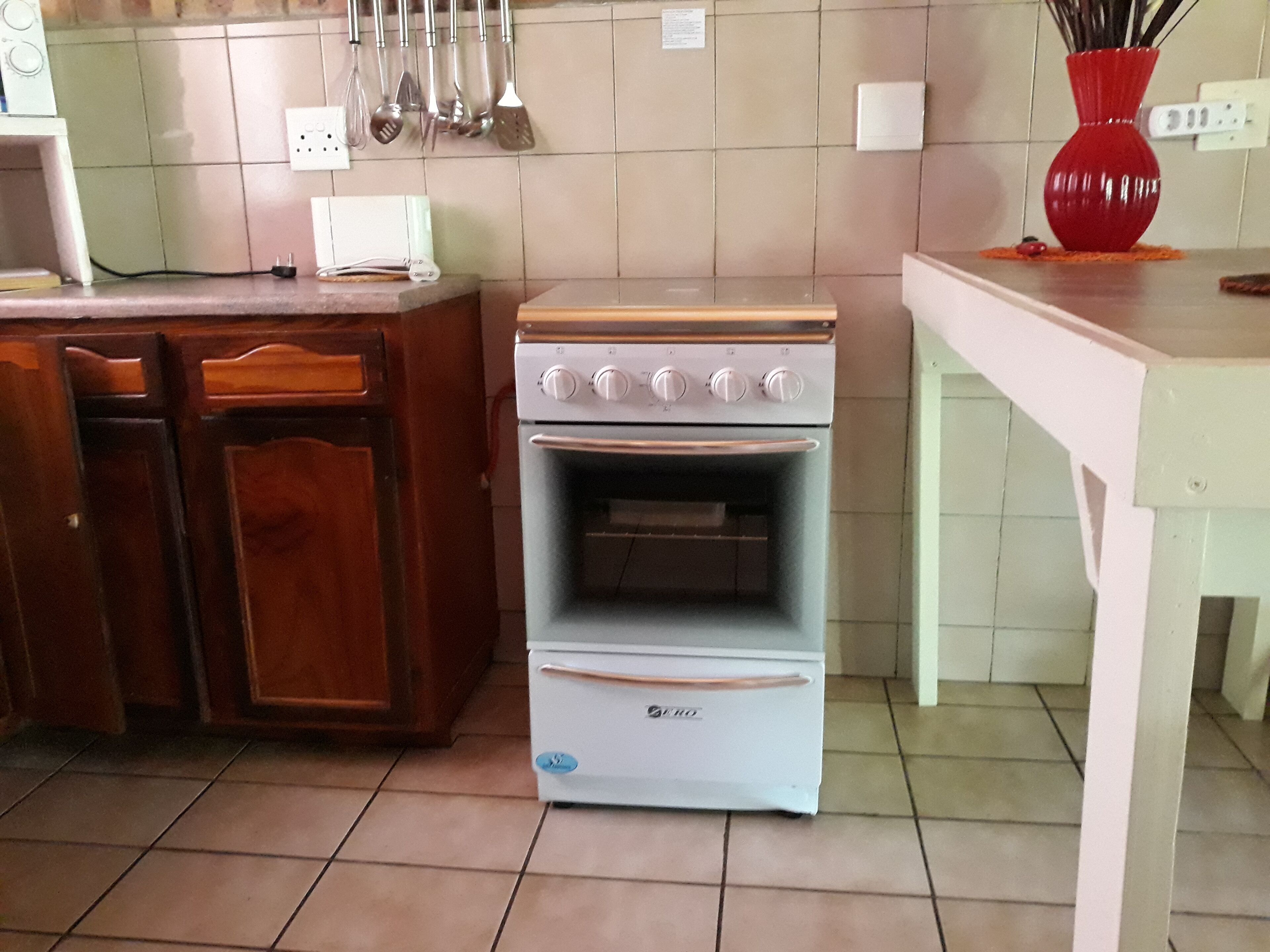 Cozinha com forno branco, armários de madeira e um vaso vermelho na bancada.