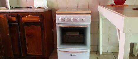 Cozinha com forno branco, armários de madeira e um vaso vermelho na bancada.