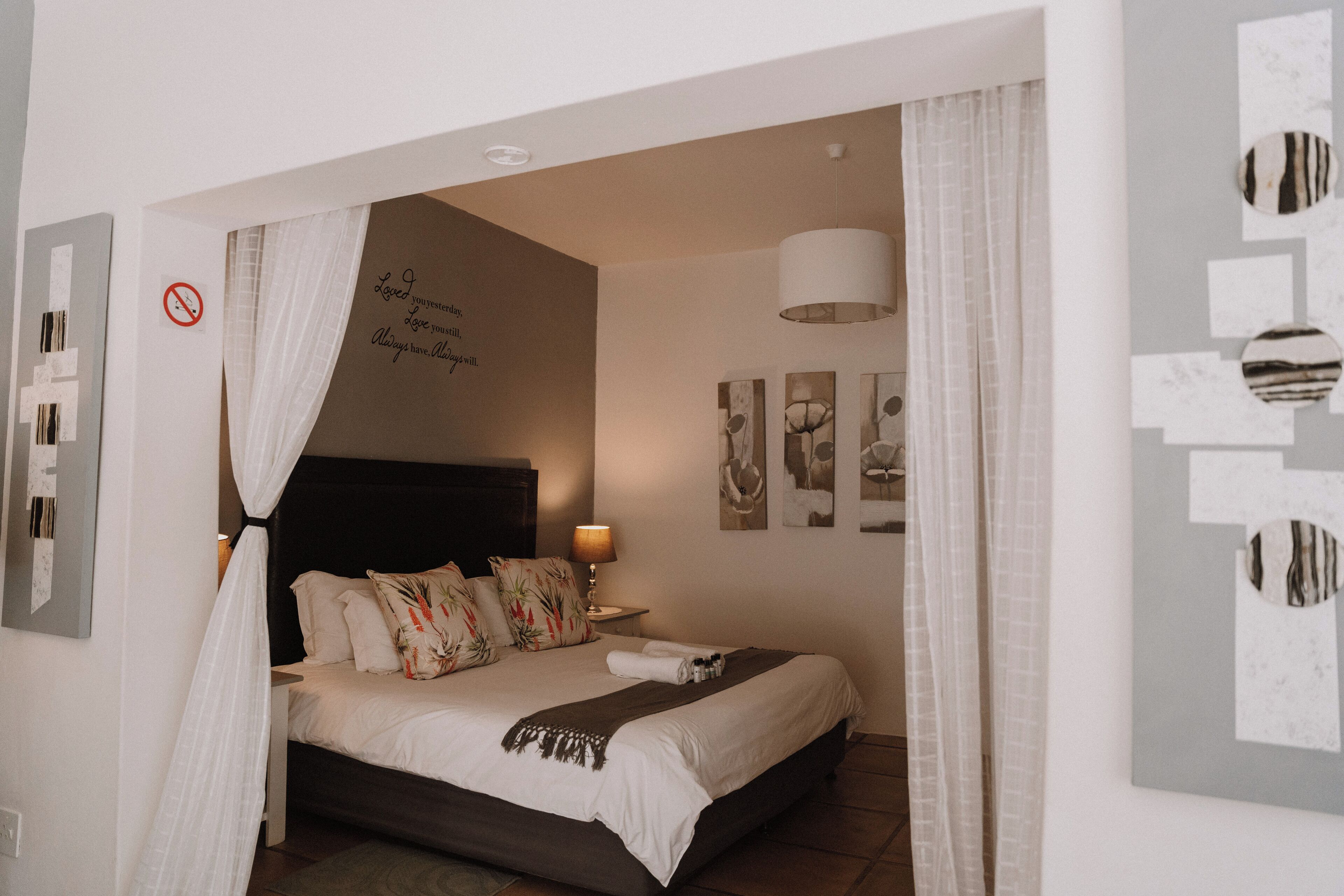Quarto com cama, mesa de cabeceira, abajur e decoração nas paredes.