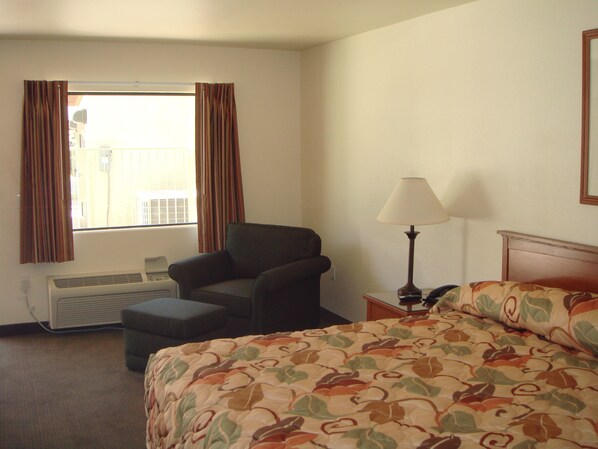 Quarto de hotel com uma cama, uma cadeira, ar condicionado, luminária e janela com cortinas.