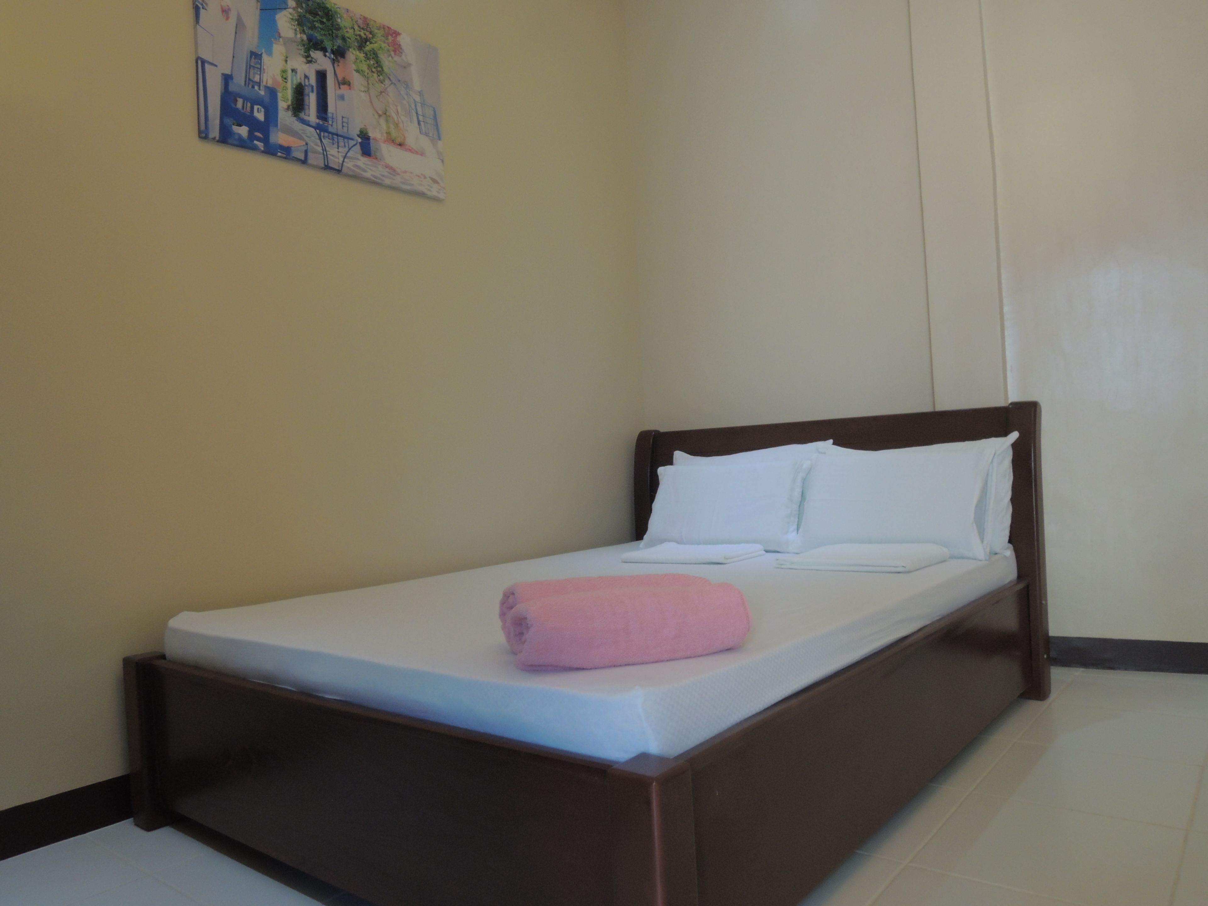 Uma cama de solteiro com estrutura de madeira, roupa de cama branca e toalha rosa.