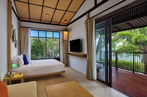 Quarto de hotel moderno com cama, TV e varanda com vista para o verde.