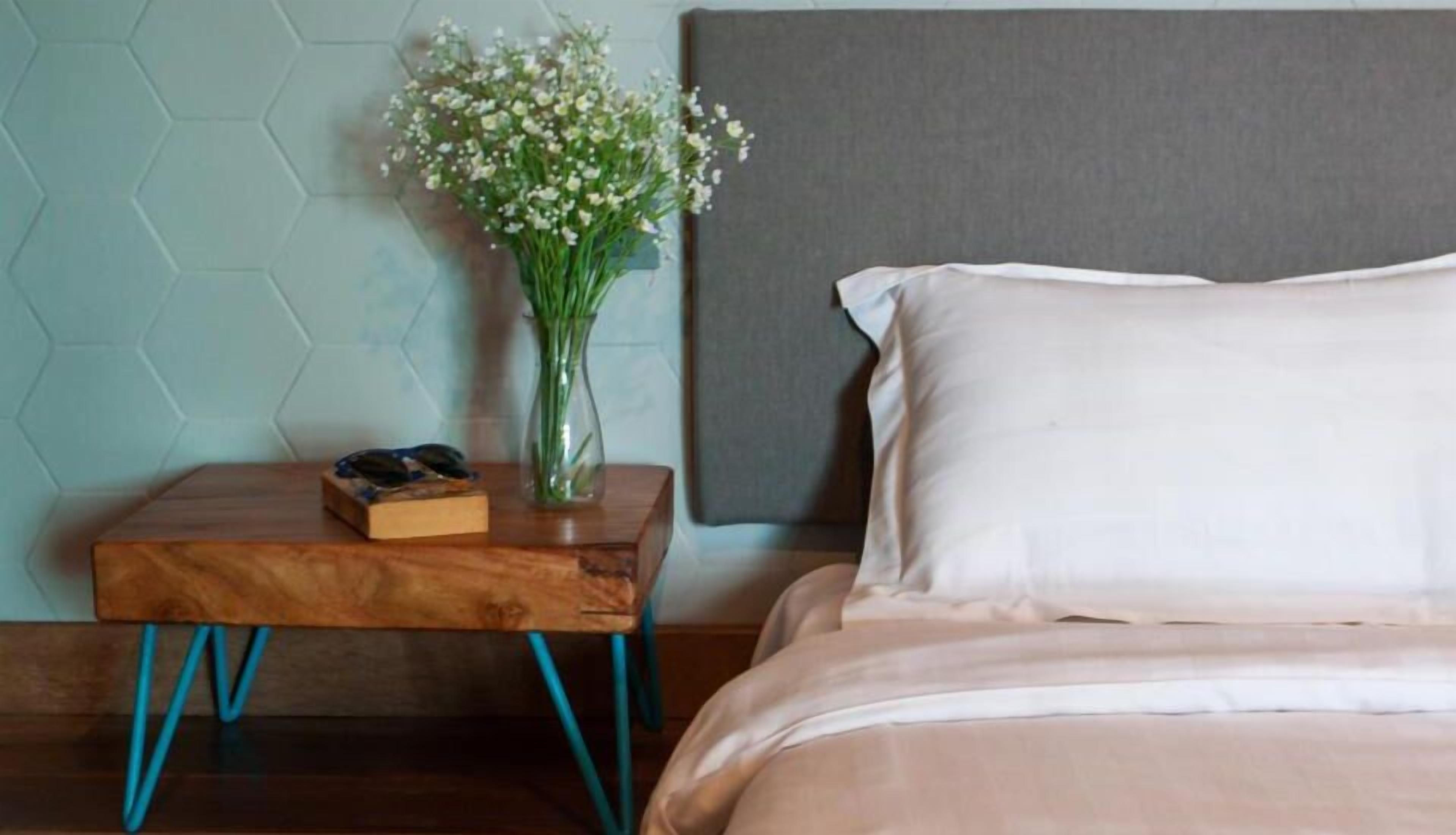 Quarto com cama, mesa de cabeceira, vaso com flores e um padrão de parede hexagonal.