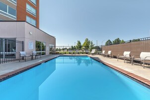 Piscina com espreguiçadeiras e um edifício com uma placa que diz 'Pool Rules'.