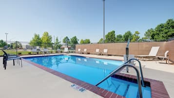 Uma piscina com borda de tijolos, escada de metal e espreguiçadeiras.