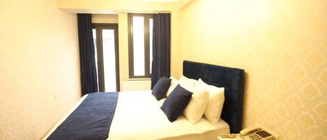 Quarto de hotel com uma cama, telefone ao lado e janela com cortinas.